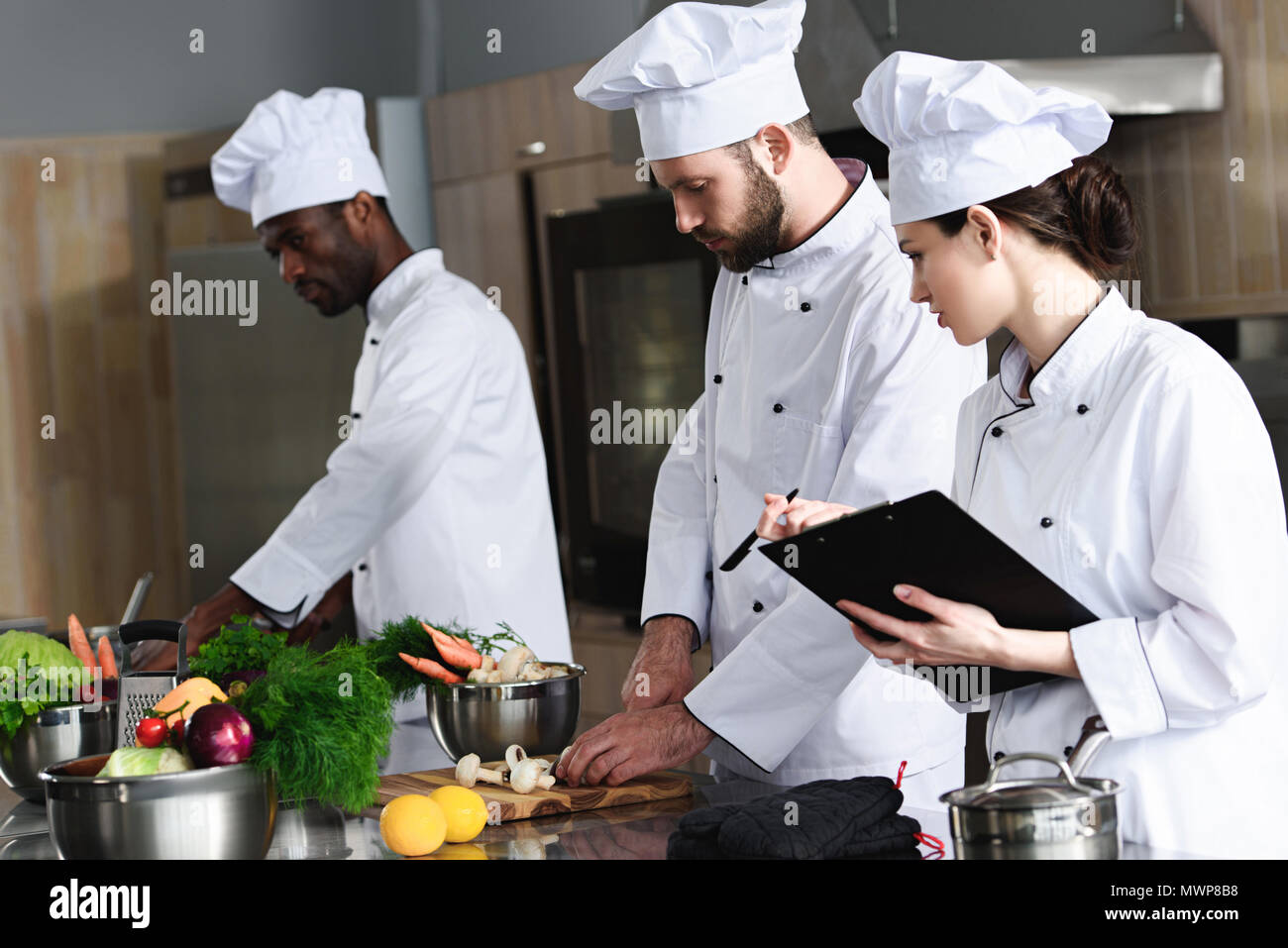Female chef writing down recipe by her multiracial colleagues Stock ...
