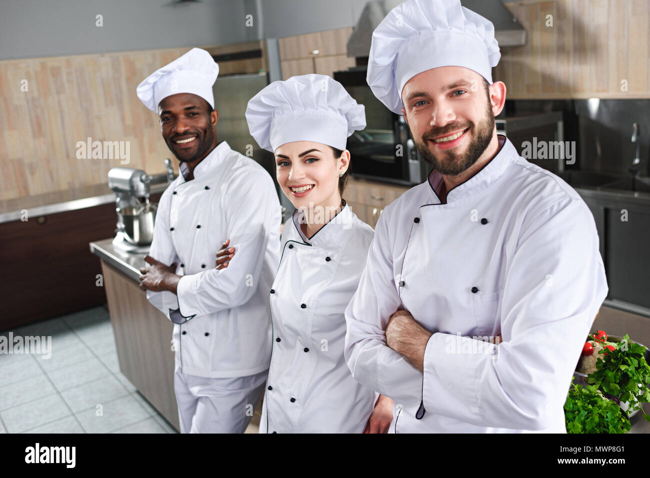 Multiracial team of cooks looking at camera by cooking table Stock ...