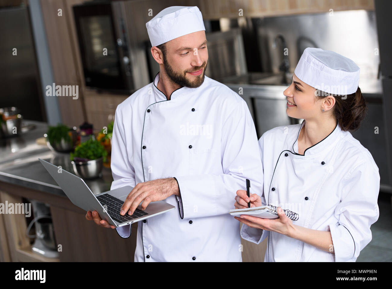 chefs using laptop at restaurant kitchen and looking at each other ...