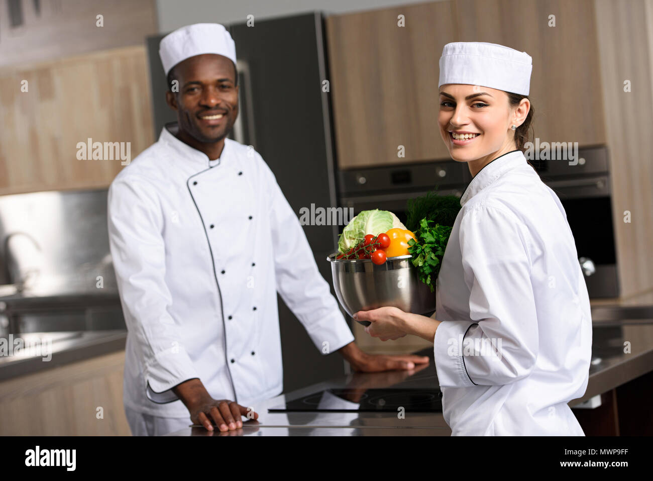 multicultural chefs holding vegetables and looking at camera at ...