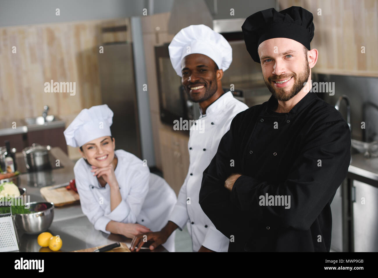 smiling multicultural chefs looking at camera at restaurant kitchen ...