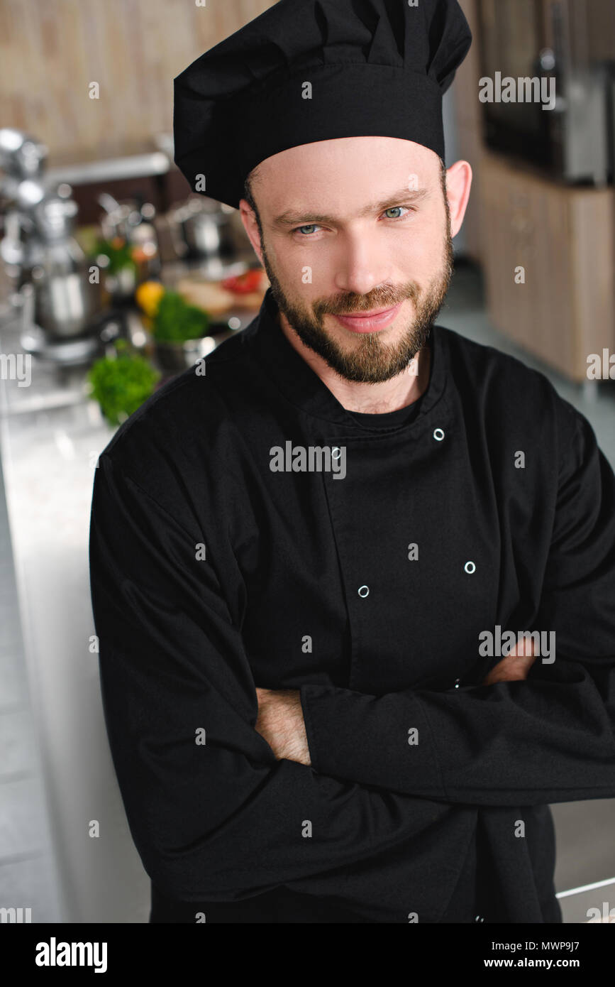 handsome chef standing with crossed arms and looking away at restaurant ...