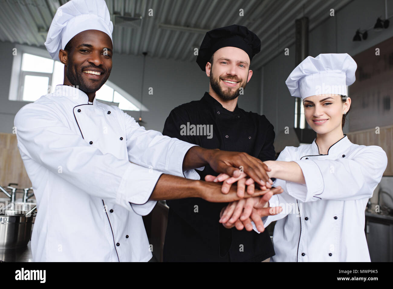 smiling multicultural chefs putting hands together at restaurant ...