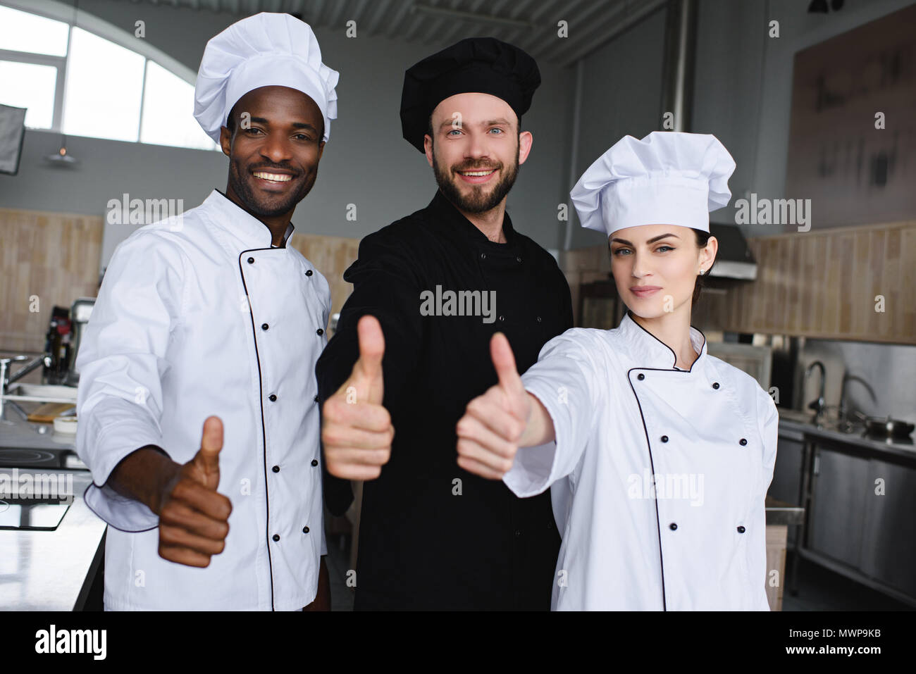 smiling multicultural chefs showing thumbs up at restaurant kitchen ...