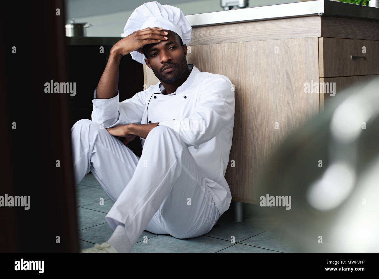 exhausted african american chef sitting on floor at restaurant kitchen ...