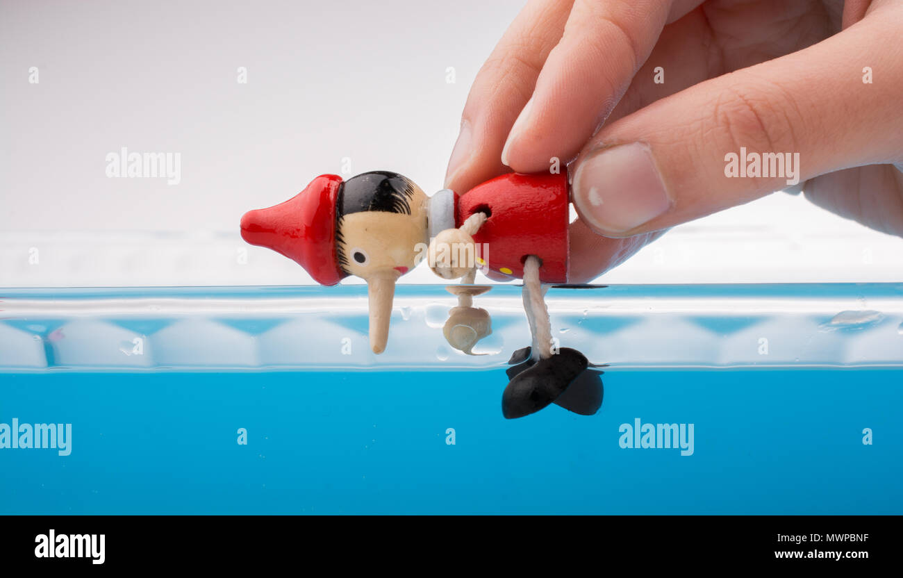 Hand holding wodden puppet Pinocchio on in blue water Stock Photo - Alamy