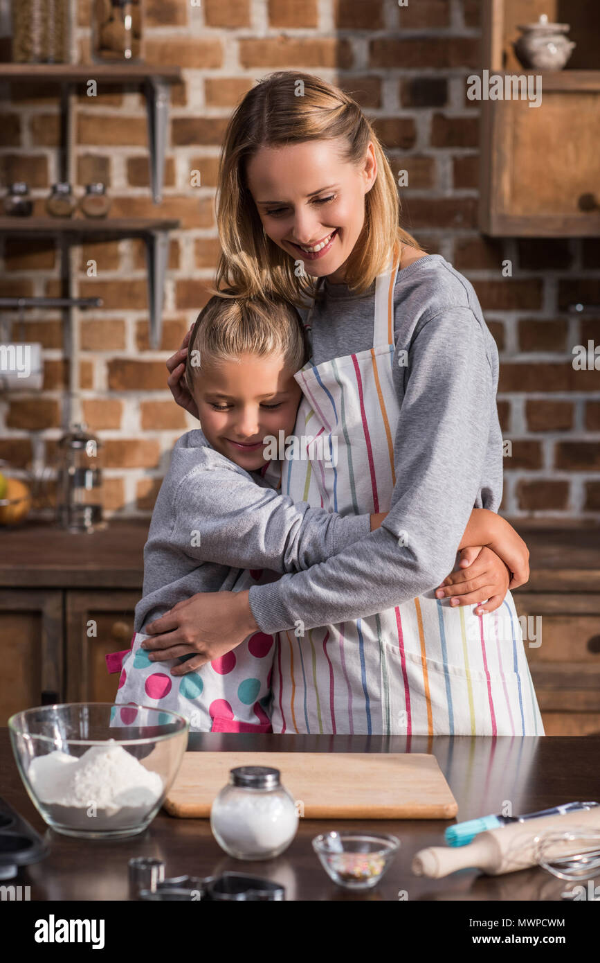 portrait of happy girl and mother hugging each other while cooking ...