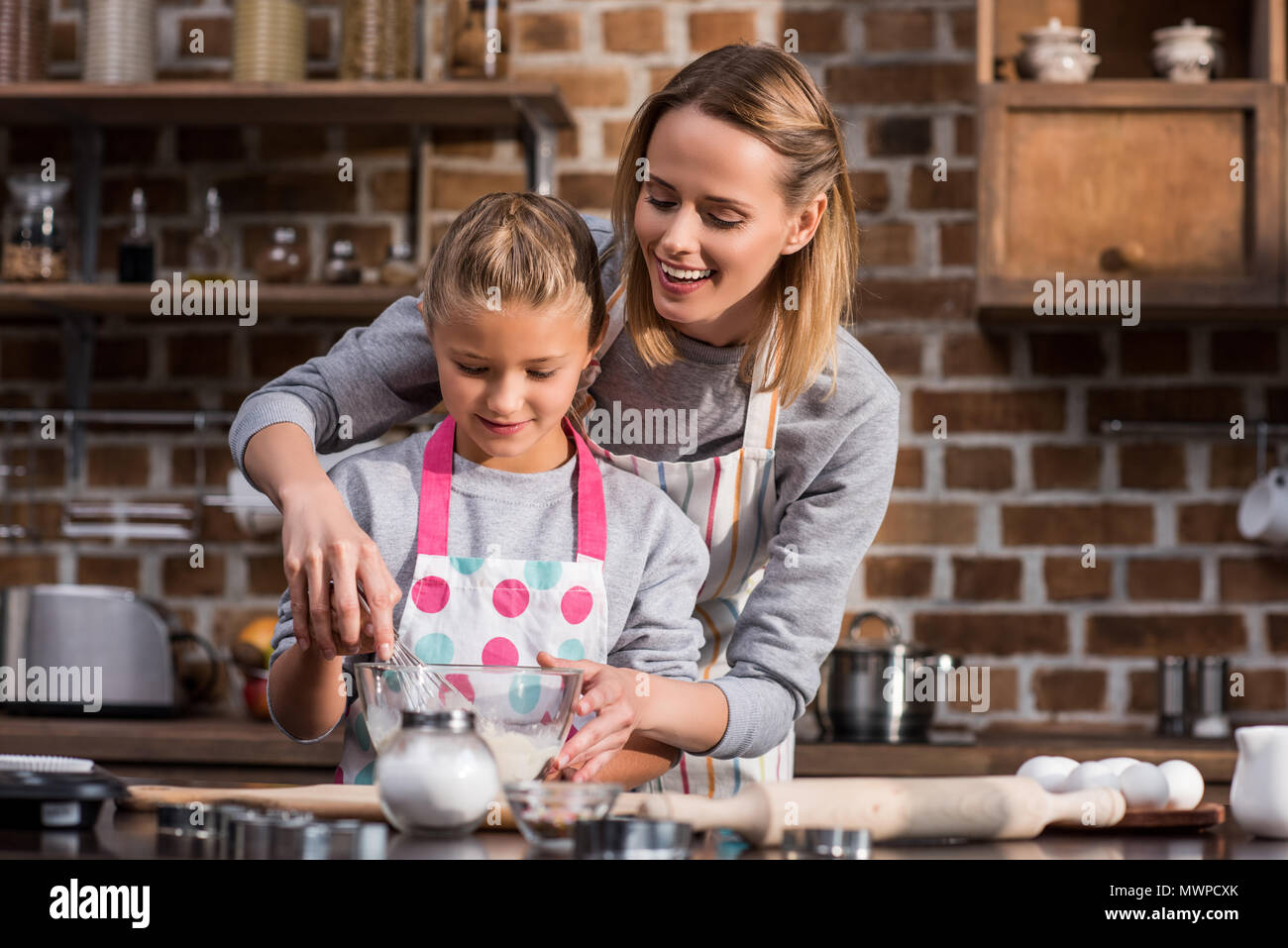 mother helping little daughter while making cookies together at home ...