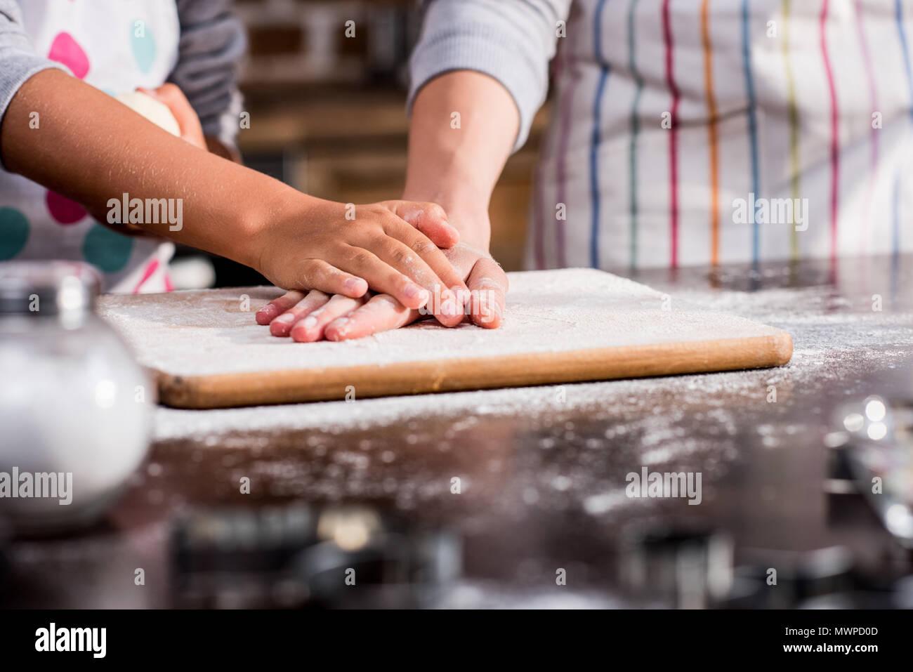partial view of family holding hands on raw dough while cooking ...