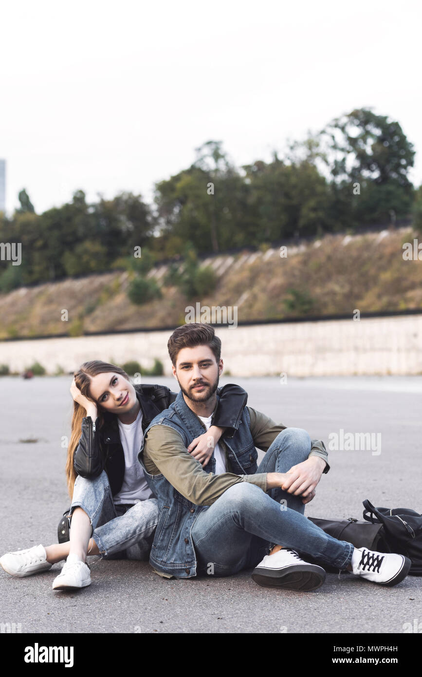 stylish couple looking at camera while resting on ground together Stock ...