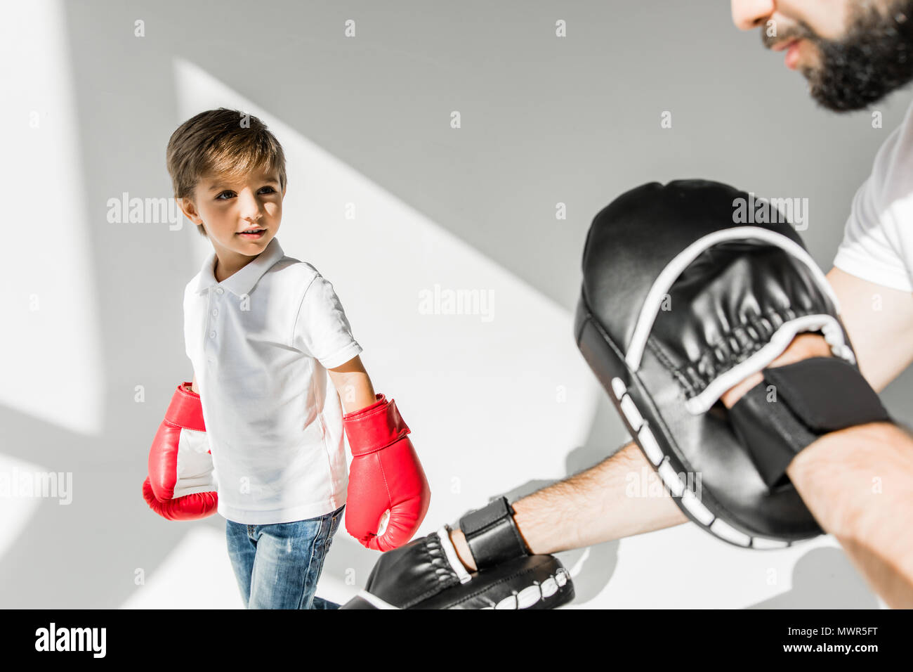cropped shot of father training cute little son in boxing gloves on ...