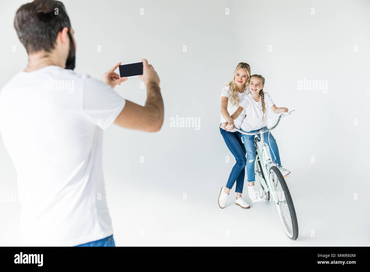 man photographing family with smartphone while child riding bicycle ...