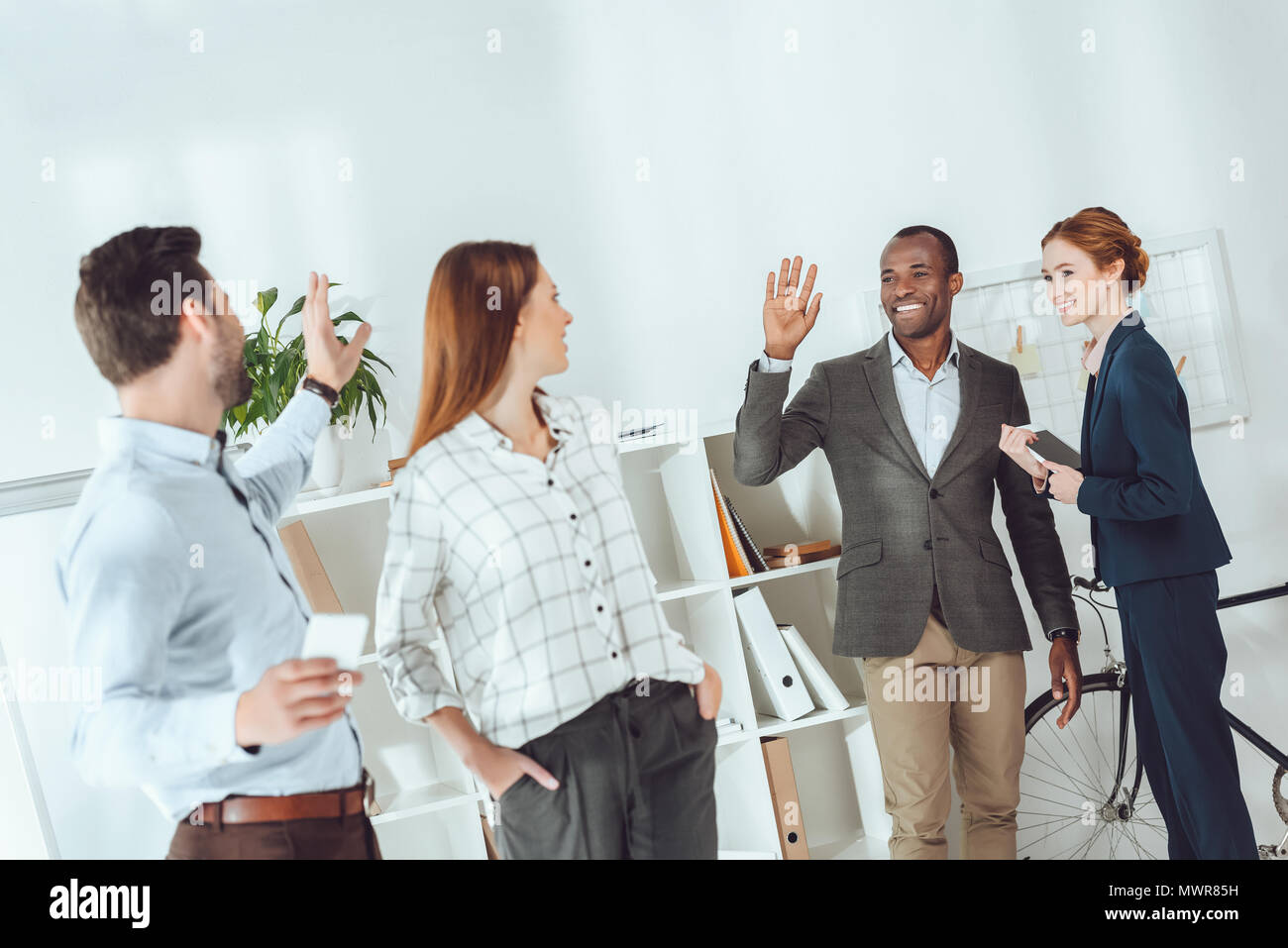 smiling multicultural businesspeople waving hands in office Stock Photo ...