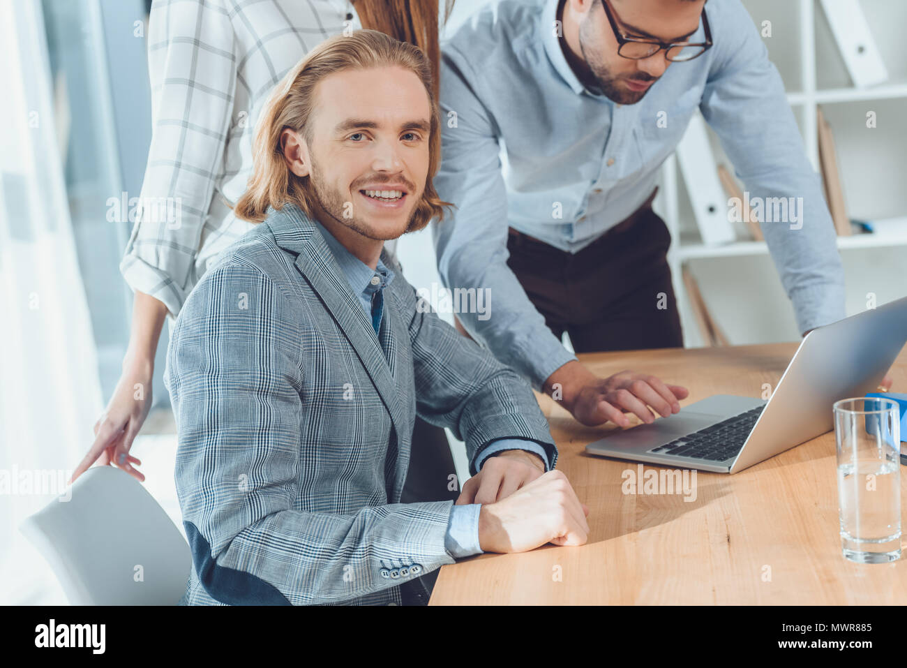 man smiling to camera while other people looking at laptop on table ...