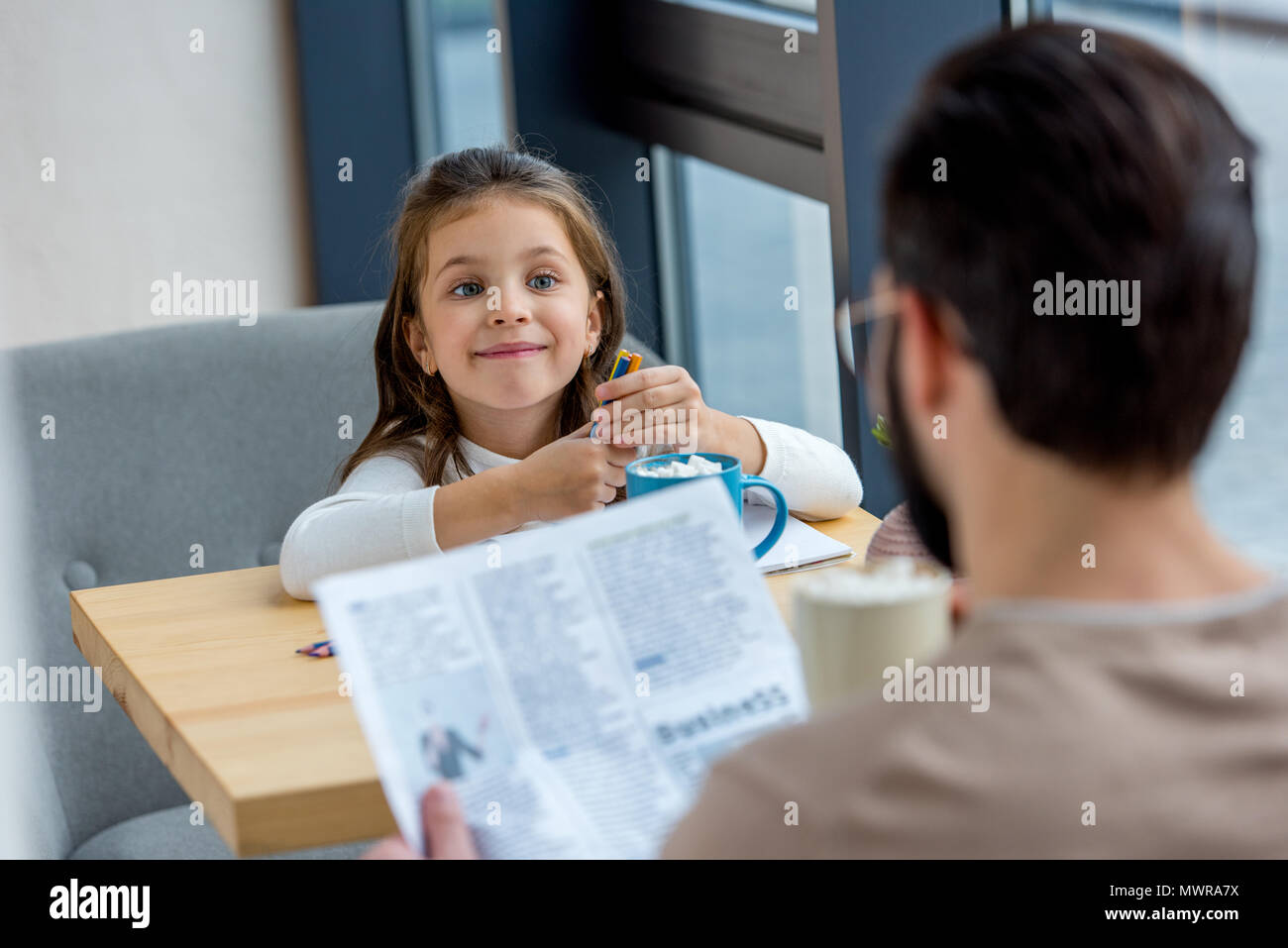 father reading business newspaper while daughter drawing in cafe Stock ...