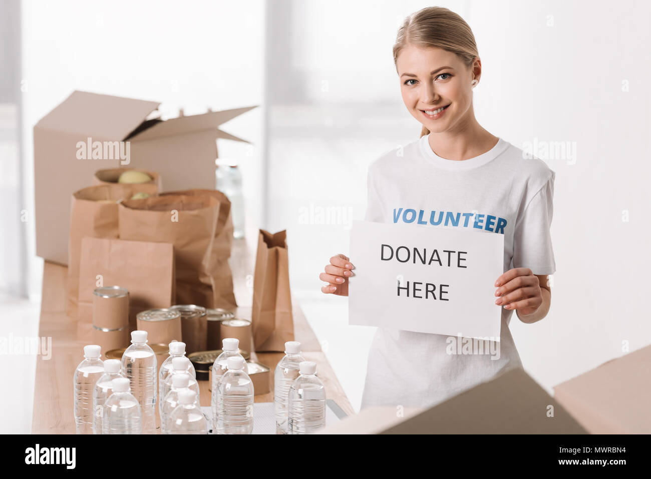 happy young female volunteer with charity placard next to table with ...