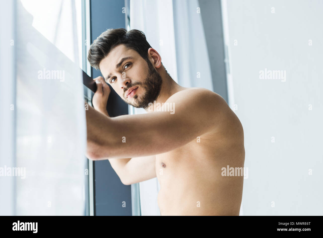 shirtless man standing at window and looking at camera Stock Photo - Alamy