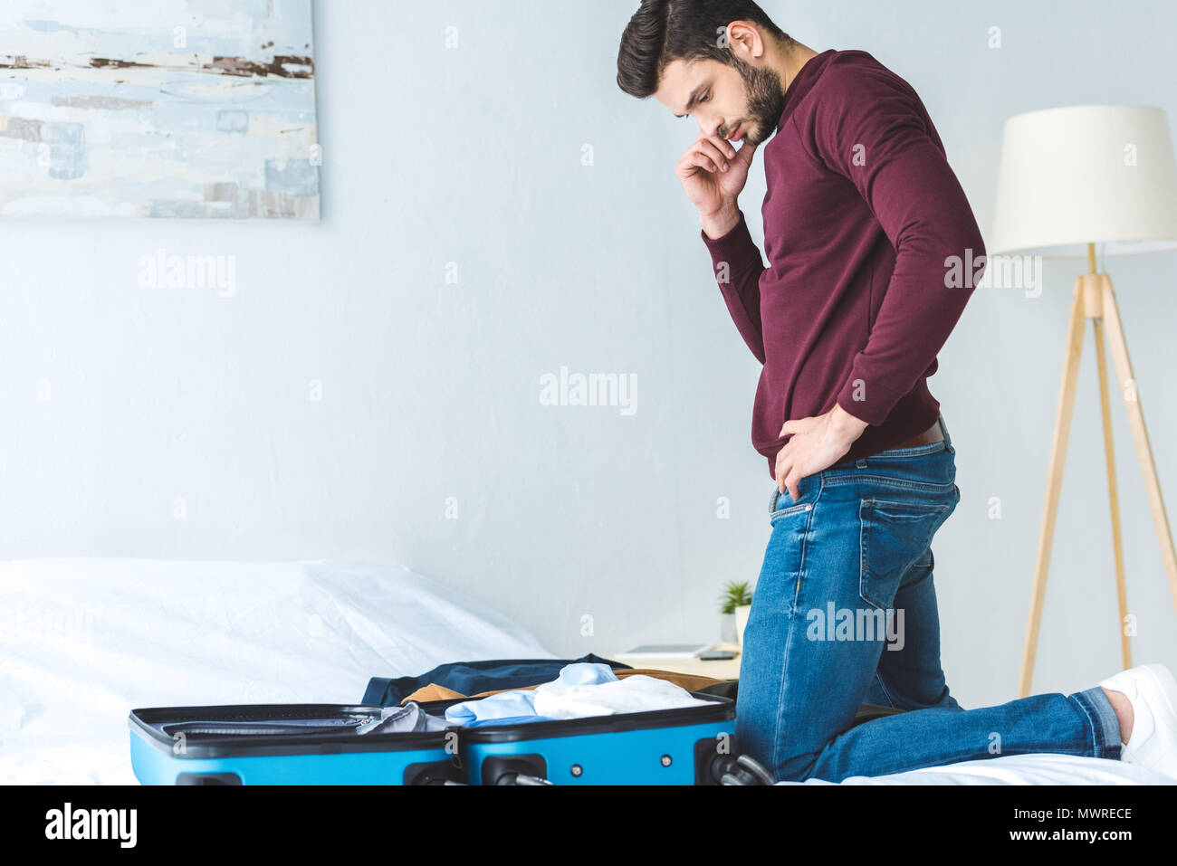 thoughtful young man packing luggage on bed for travel Stock Photo - Alamy
