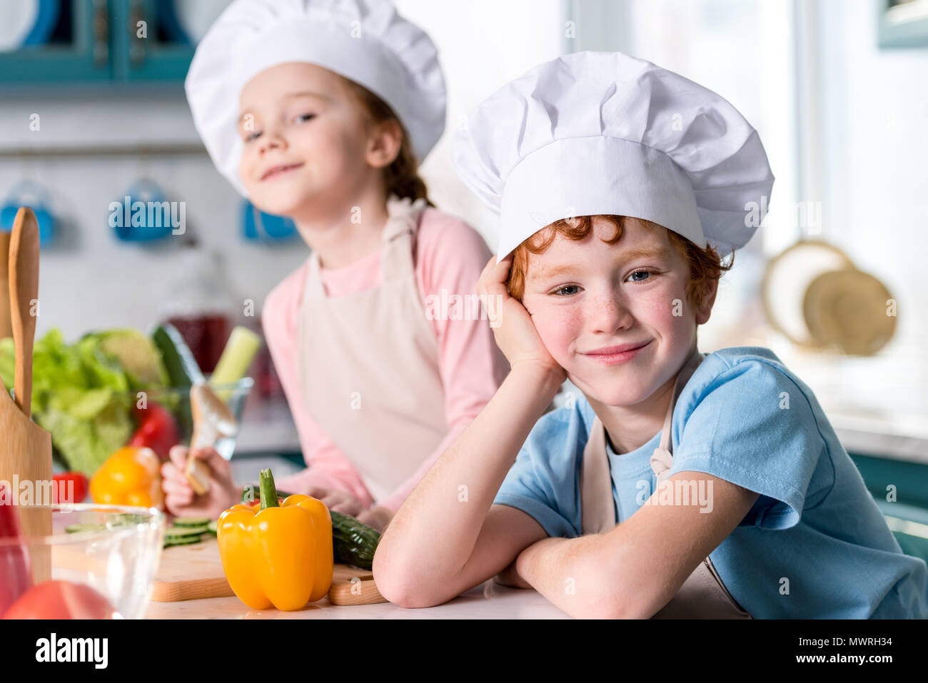 adorable siblings in chef hats and aprons smiling at camera while ...