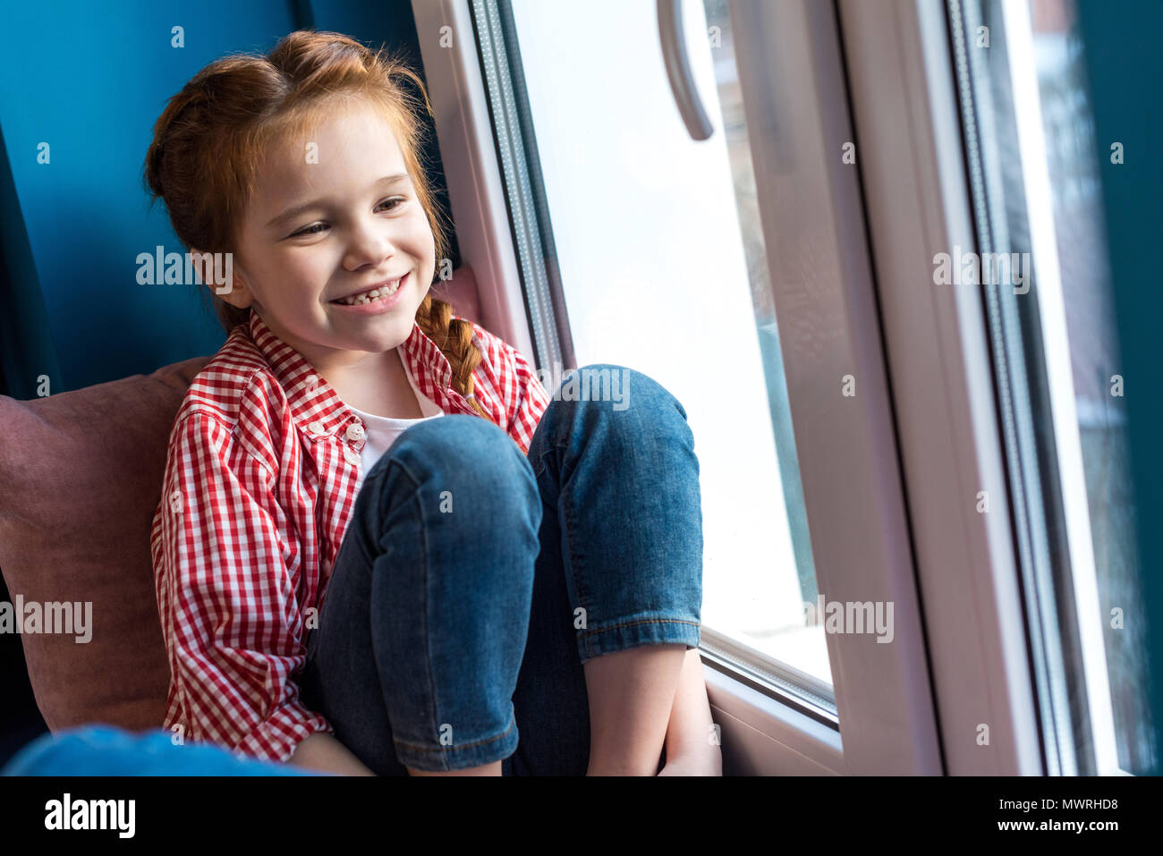 beautiful happy little child sitting in windowsill and looking away ...
