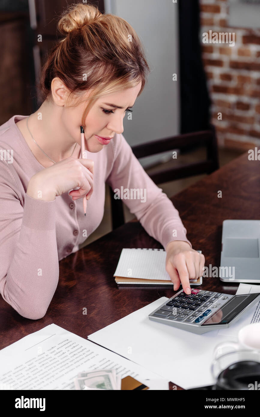 side view of woman making calculations at table at home, financial ...