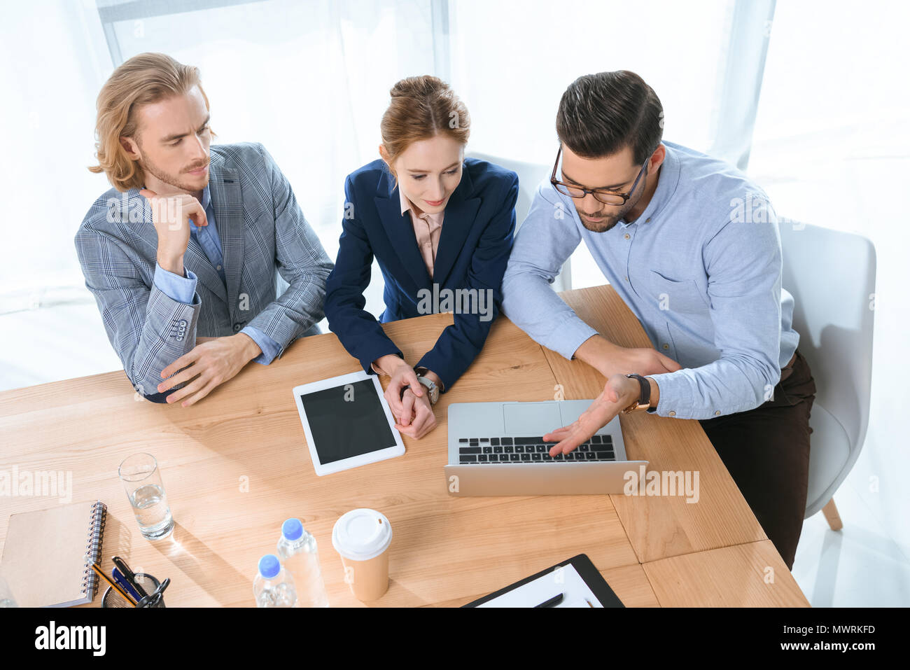 man in blue shirt pointing on laptop on table to team at office space ...