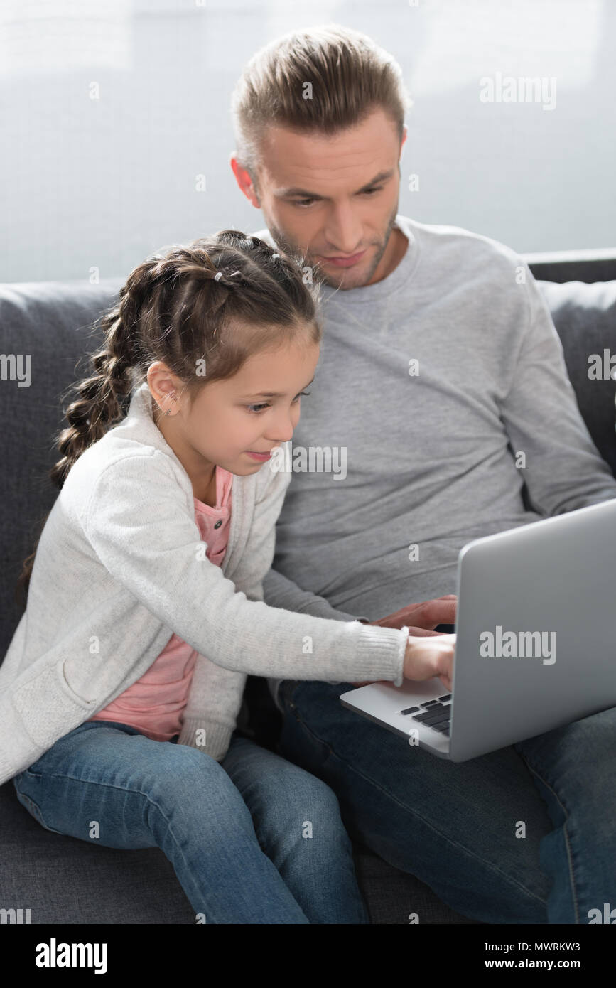 Father and daughter looking something at laptop while sitting on sofa ...
