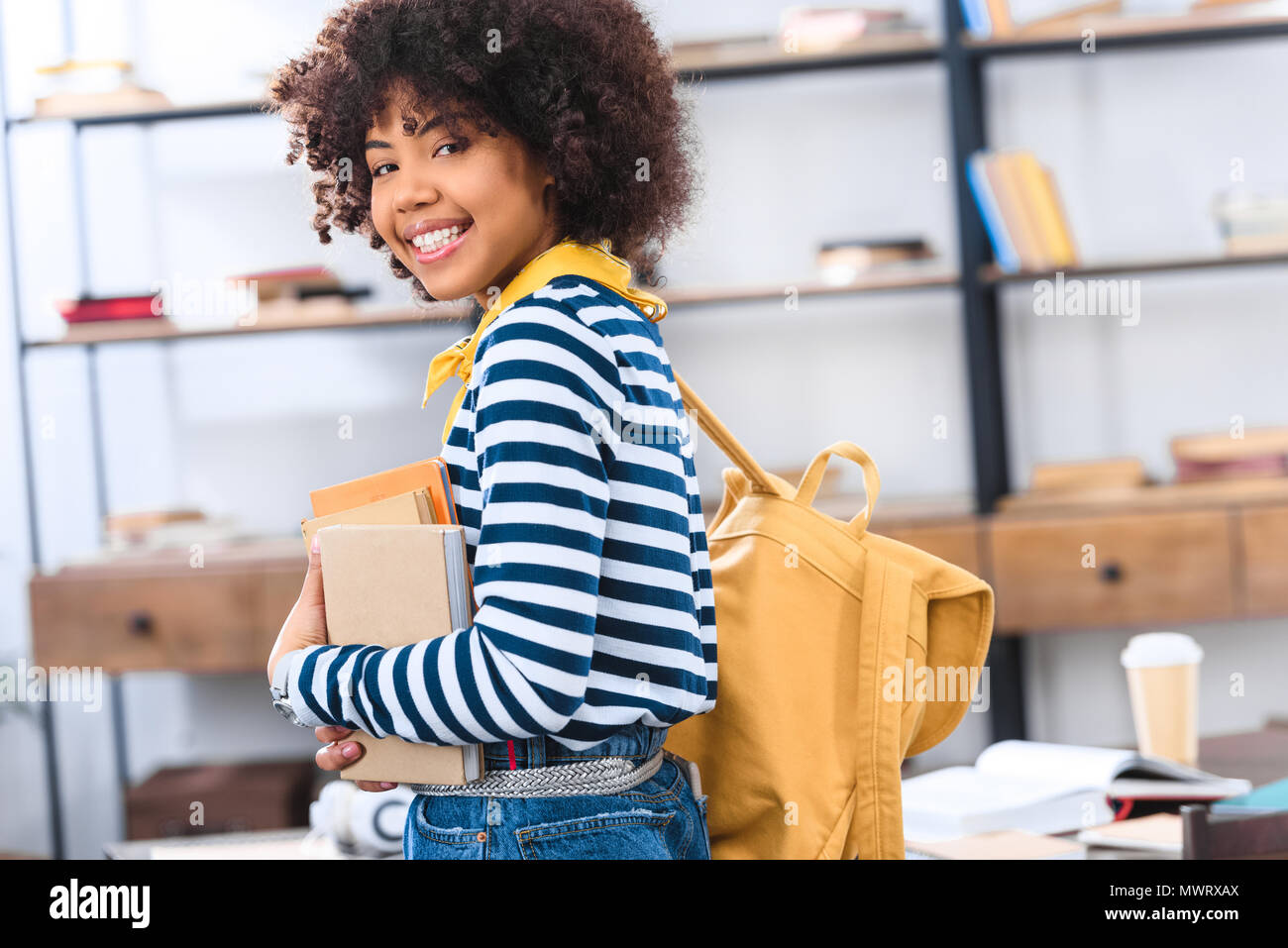 side view of smiling african american student with books and backpack ...