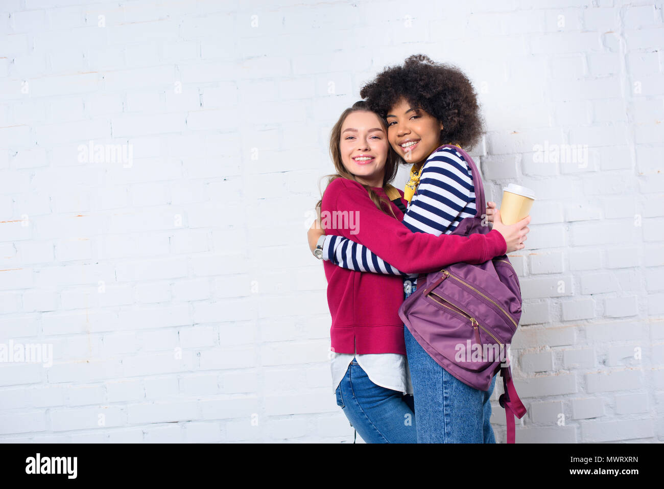 portrait of cheerful multicultural students hugging each other against ...