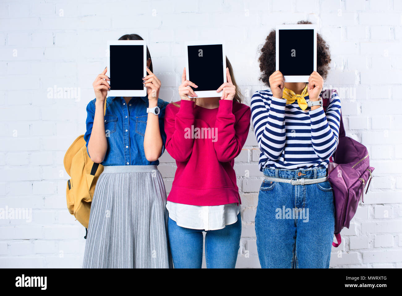 obscured view of students showing tablets with blank screens in hands ...