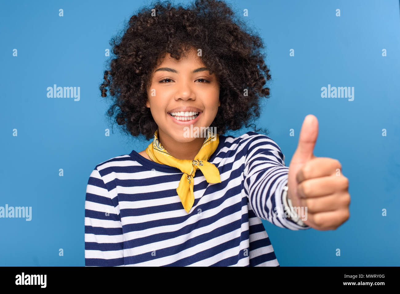 smiling african american young girl showing thumb up, isolated on blue ...