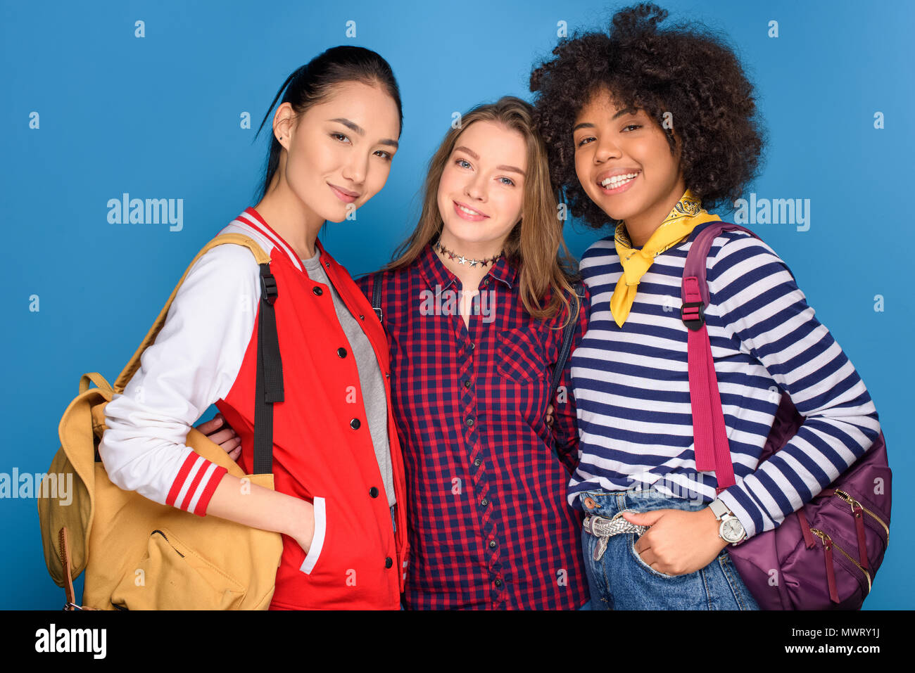 female multicultural students posing with backpacks, isolated on blue ...