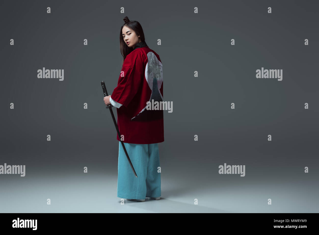 back view of samurai in kimono holding katana and looking at camera on ...