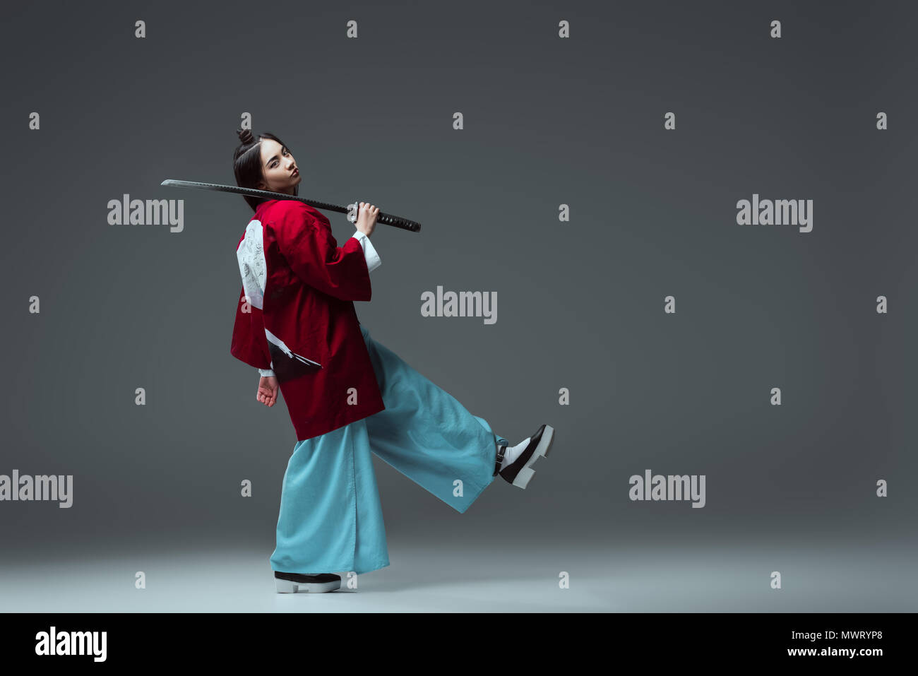 side view of samurai in kimono walking with katana and looking at ...