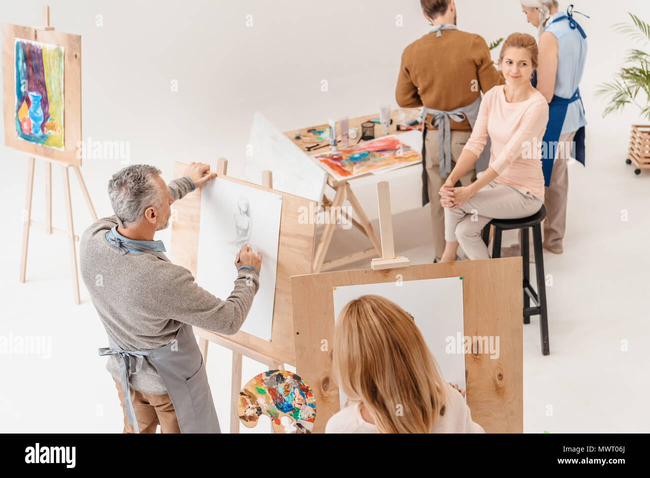 high angle view of senior students painting on easels at ast class ...
