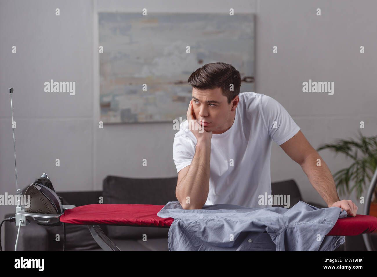 handsome man resting chin on hand and looking away in living room Stock ...