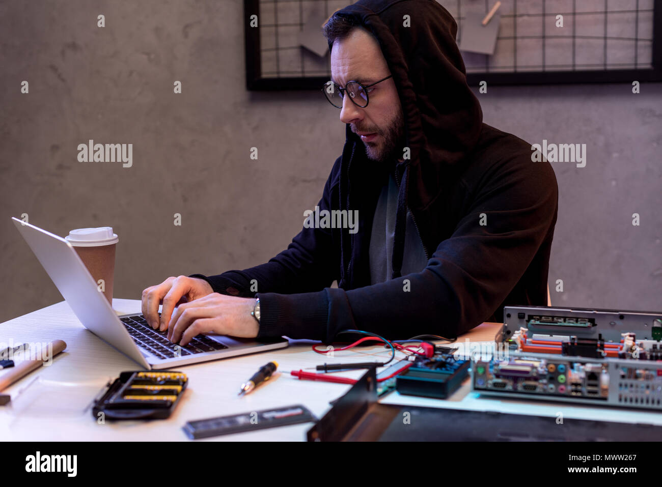man in hoodie using laptop near broken pc Stock Photo - Alamy