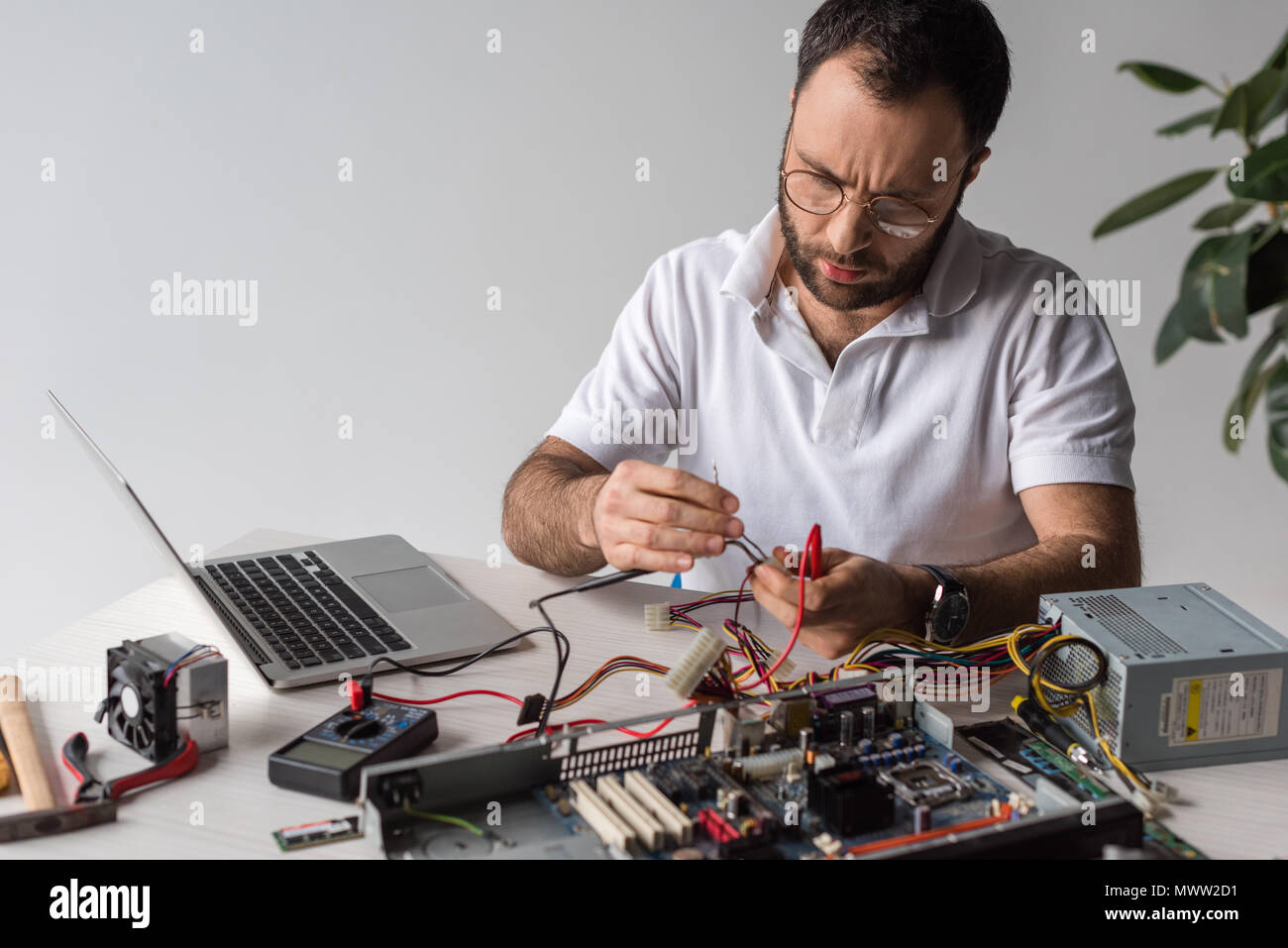 man using multimeter while fixing broken computer and looking down ...