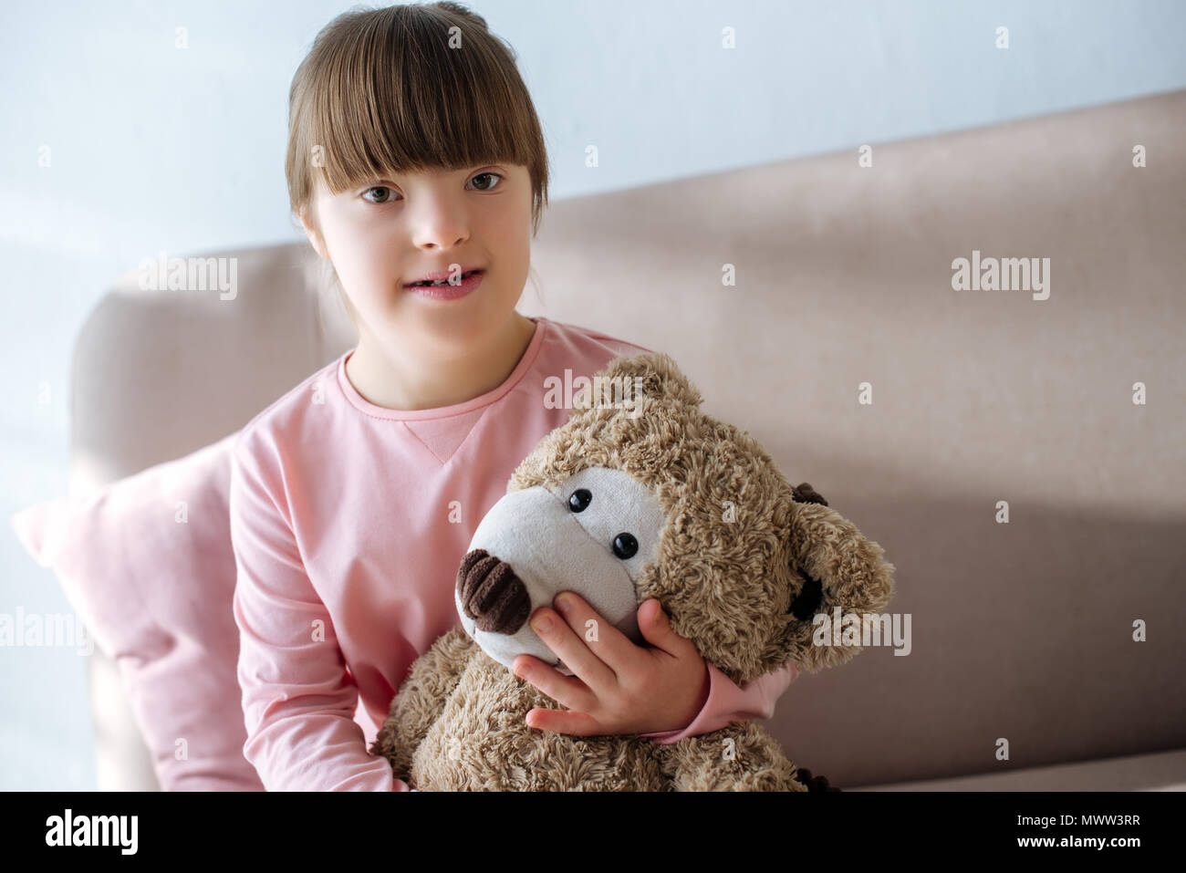 Smiling child with down syndrome sitting on sofa and holding teddy bear ...