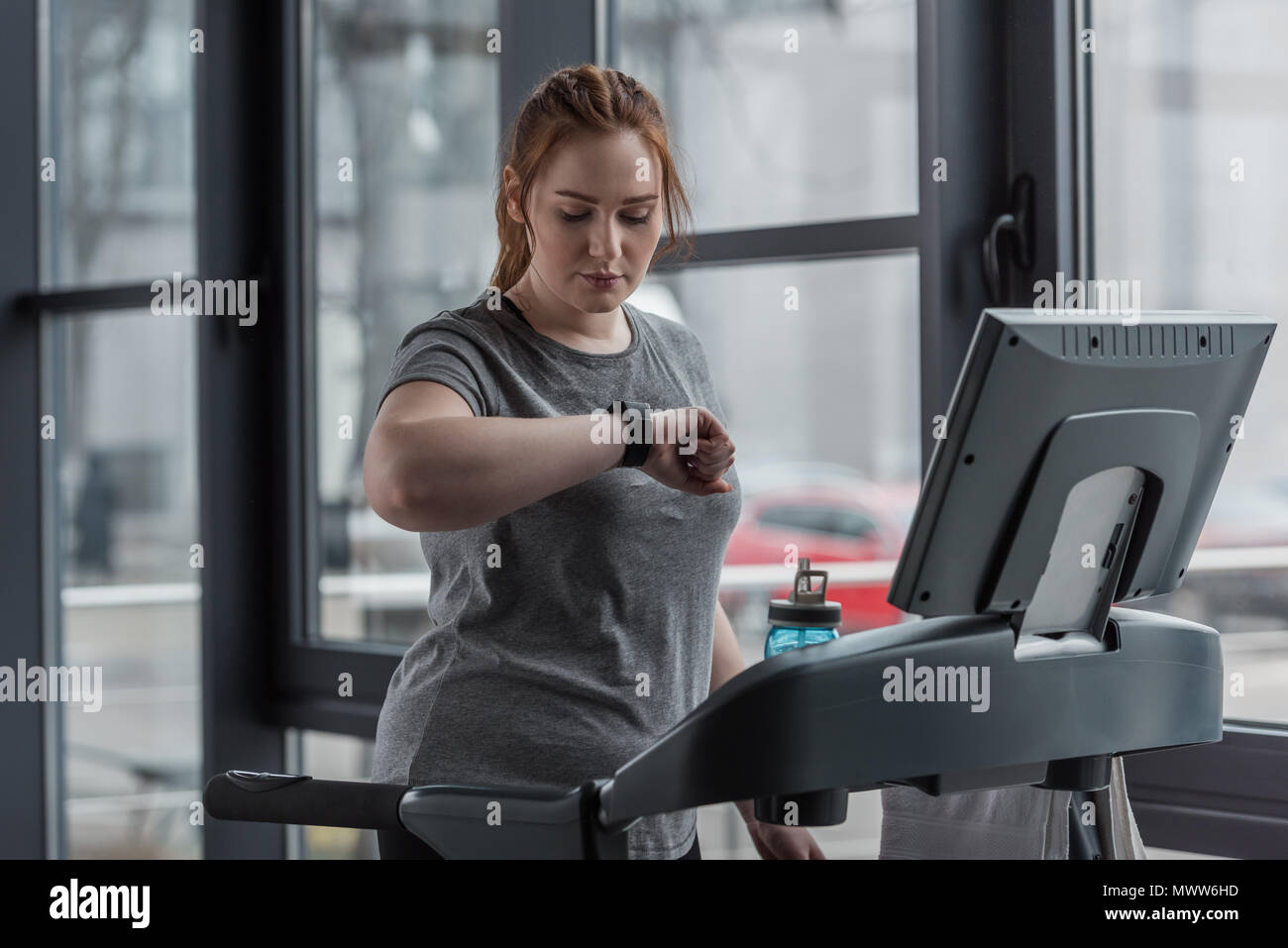 Overweight girl looking at fitness tracker while running on treadmill ...