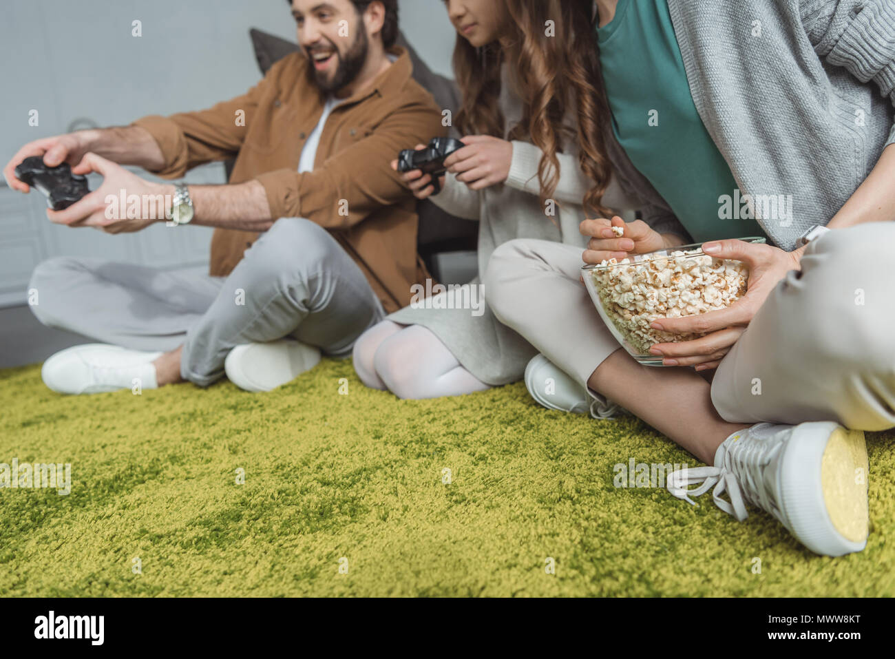 cropped image of parents and daughter playing video game and eating ...