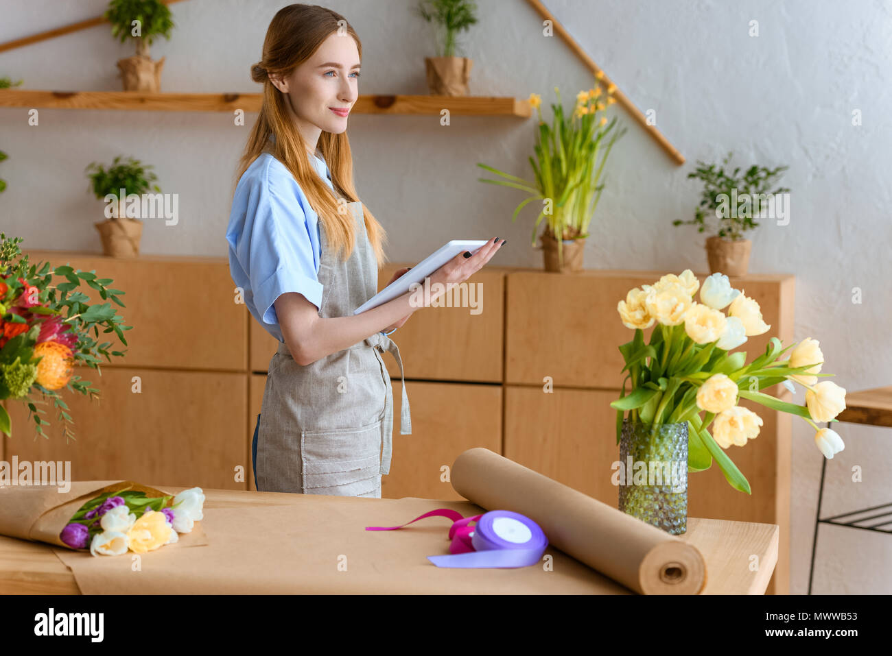 beautiful smiling young florist holding digital tablet and looking away ...