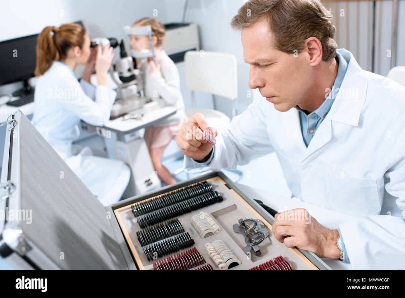 male oculist holding lenses for trial frame while colleague examining ...