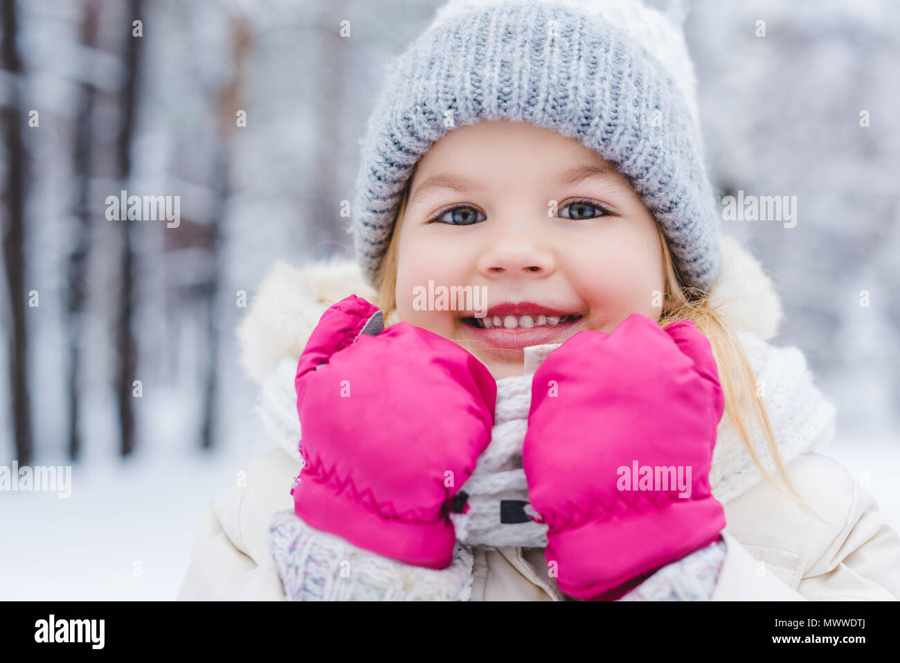 close-up portrait of cute little child in hat and mittens smiling at ...