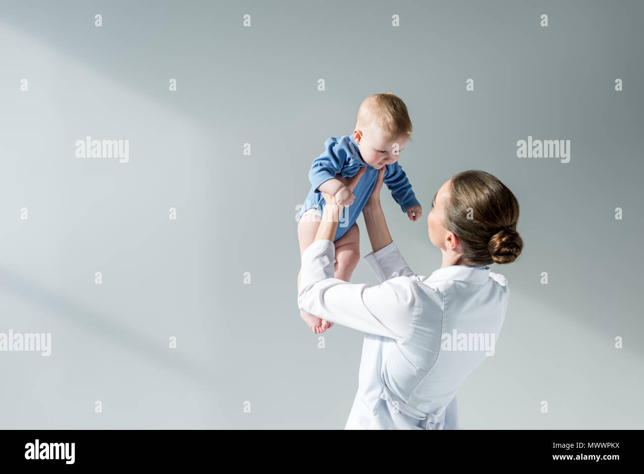 rear view of female pediatrician playing with little baby on grey Stock ...