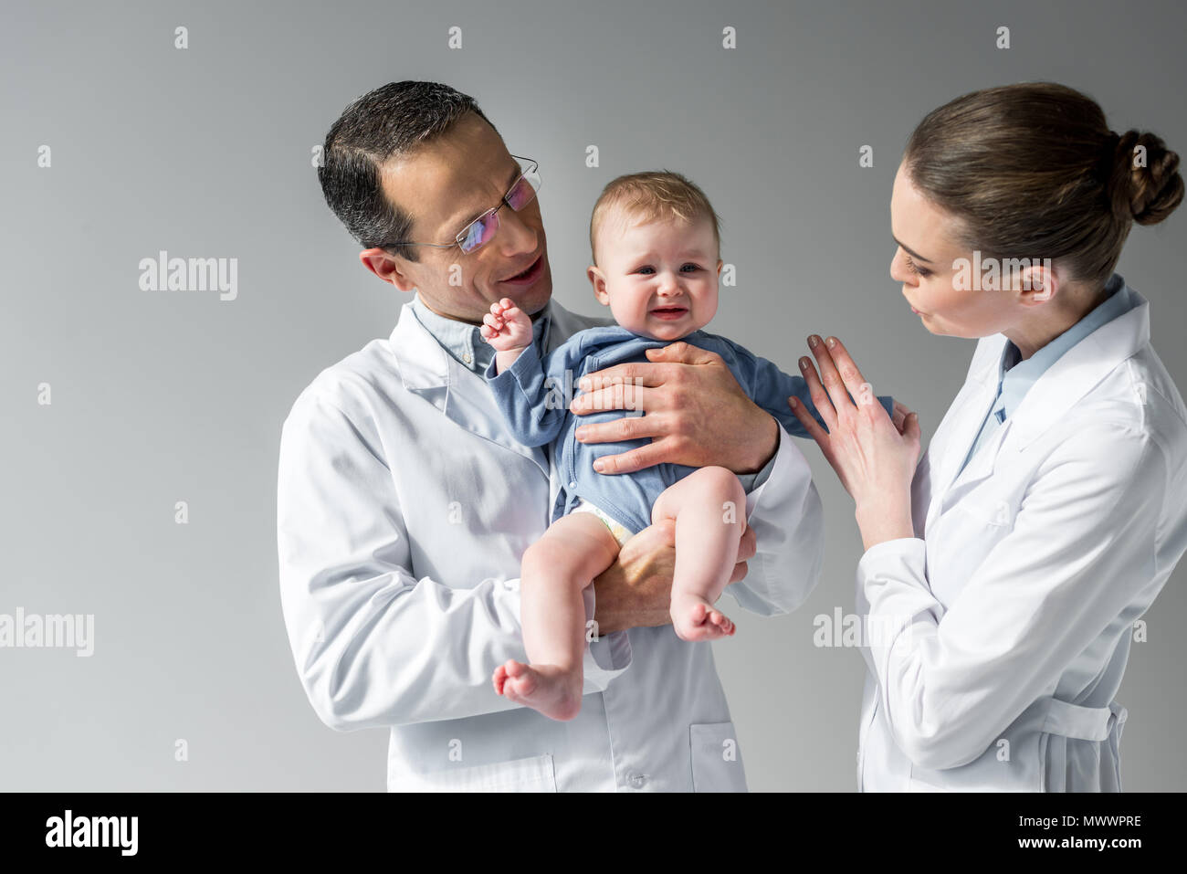 pediatricians trying to calm down little crying baby on grey Stock ...