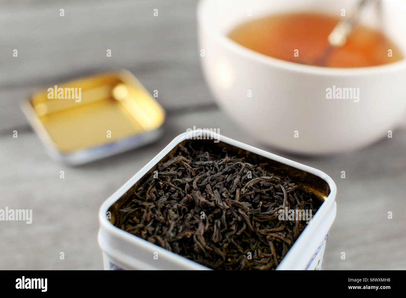 Black loose tea in metal tin, with blurred cup of hot amber drink in ...