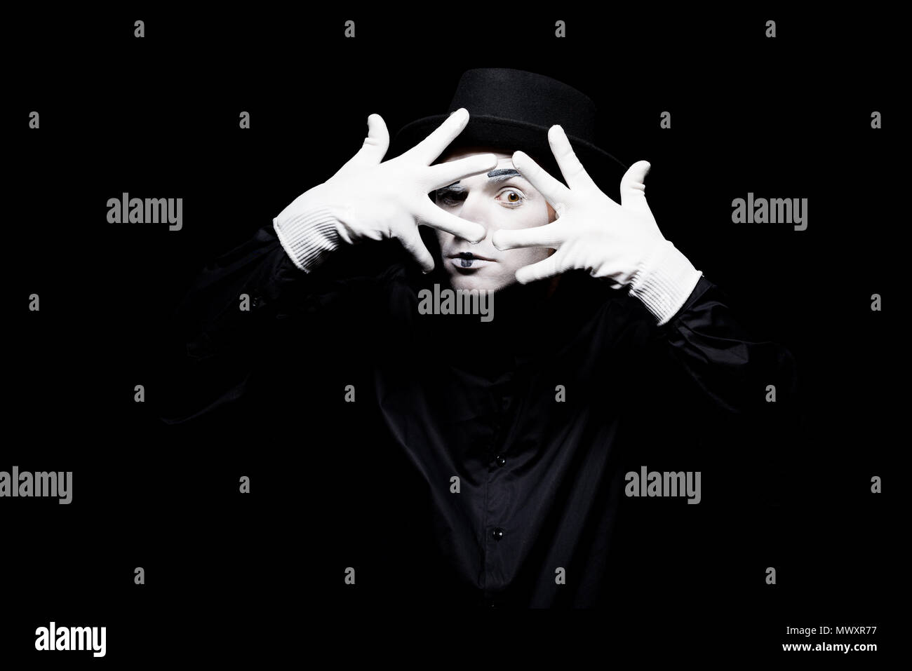 mime looking at camera through spread fingers isolated on black Stock ...
