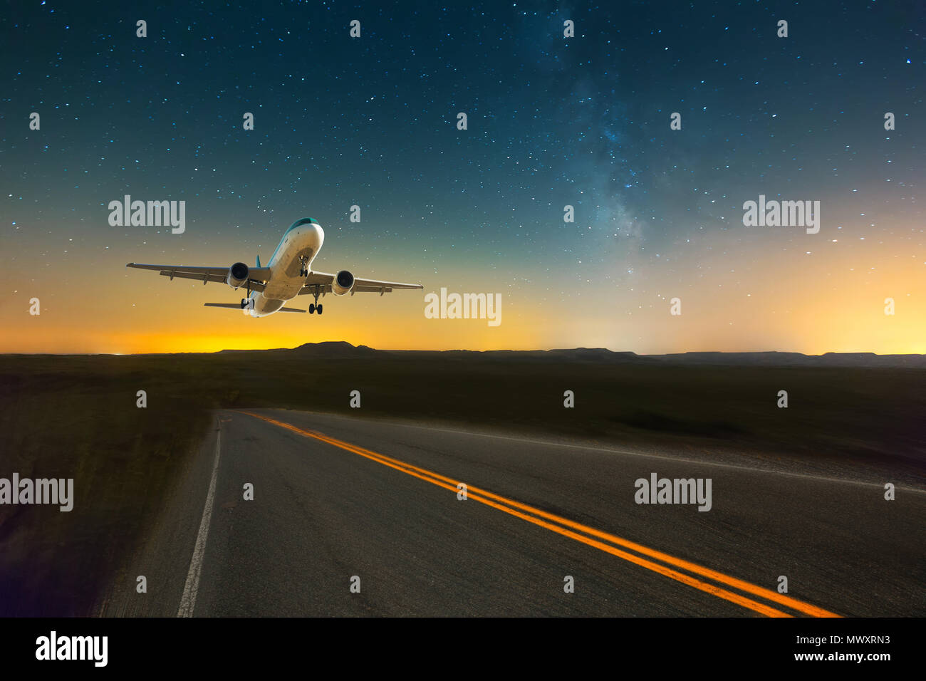 Airplane flying high in dark night sky against desert-like landscape ...