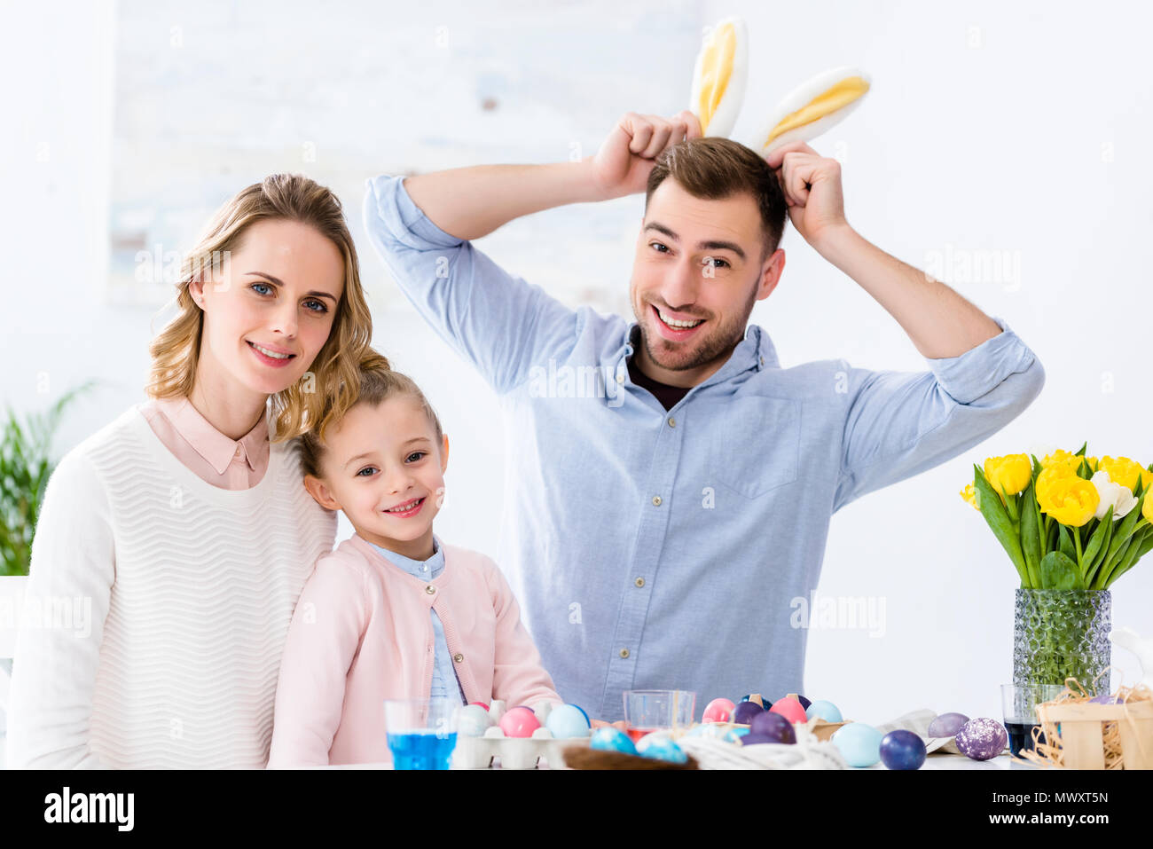Happy family playing with bunny ears by table with colored eggs for ...